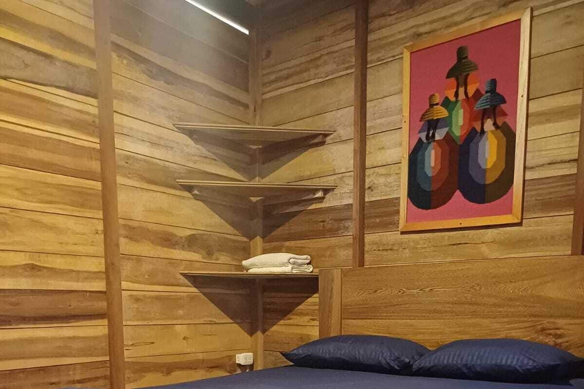 Quarto de cabana de madeira com cama, prateleira com toalha e pintura colorida na parede.