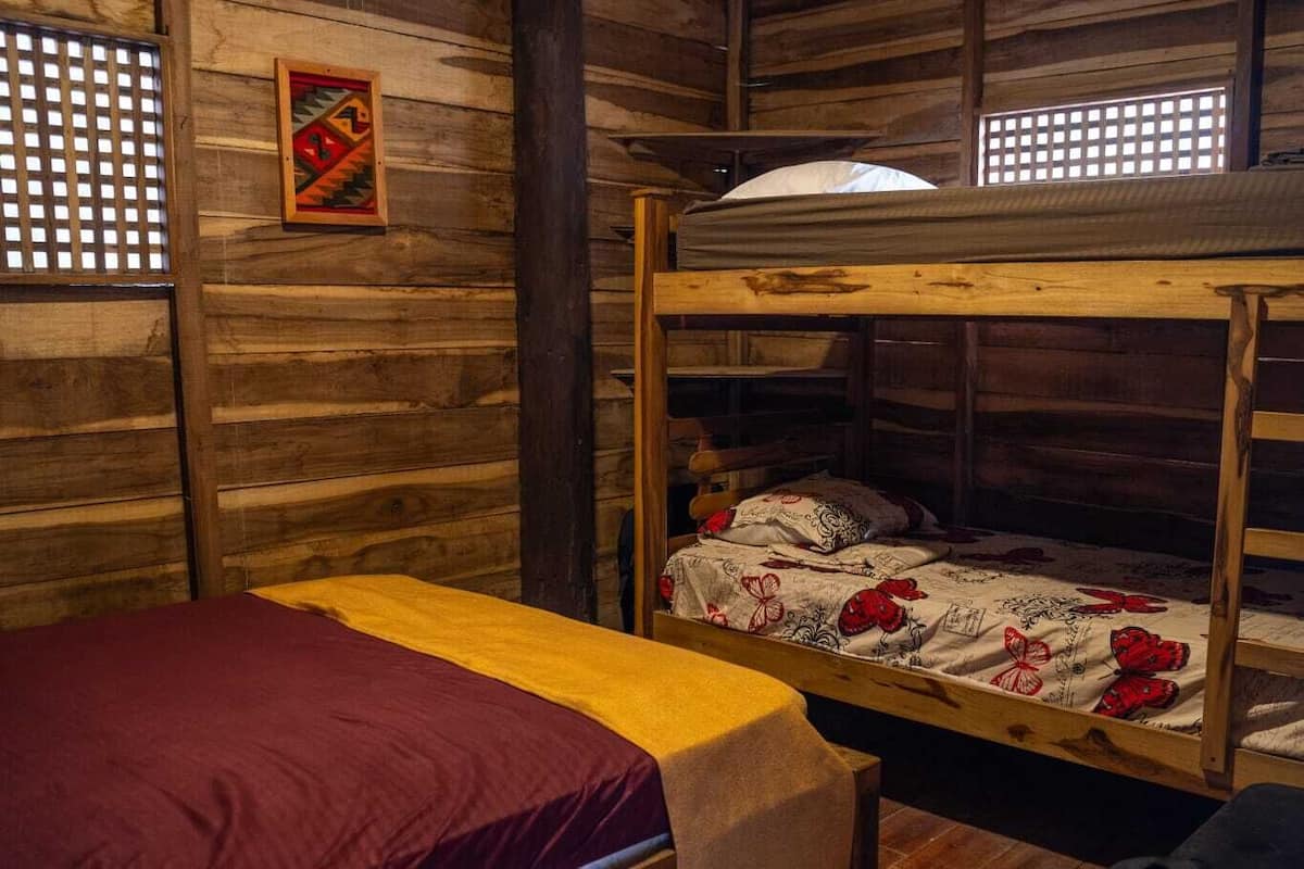 Quarto estilo cabana com cama de solteiro e uma cama individual, paredes de madeira e janela com design treliçado.