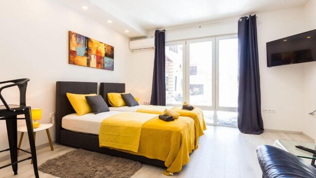 Quarto de hotel moderno com duas camas, televisão de tela plana e uma janela grande.