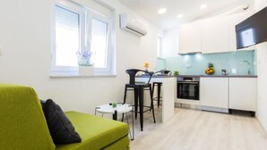 Cozinha moderna com armários brancos, forno embutido e um pequeno espaço de jantar com sofá verde e duas cadeiras pretas.