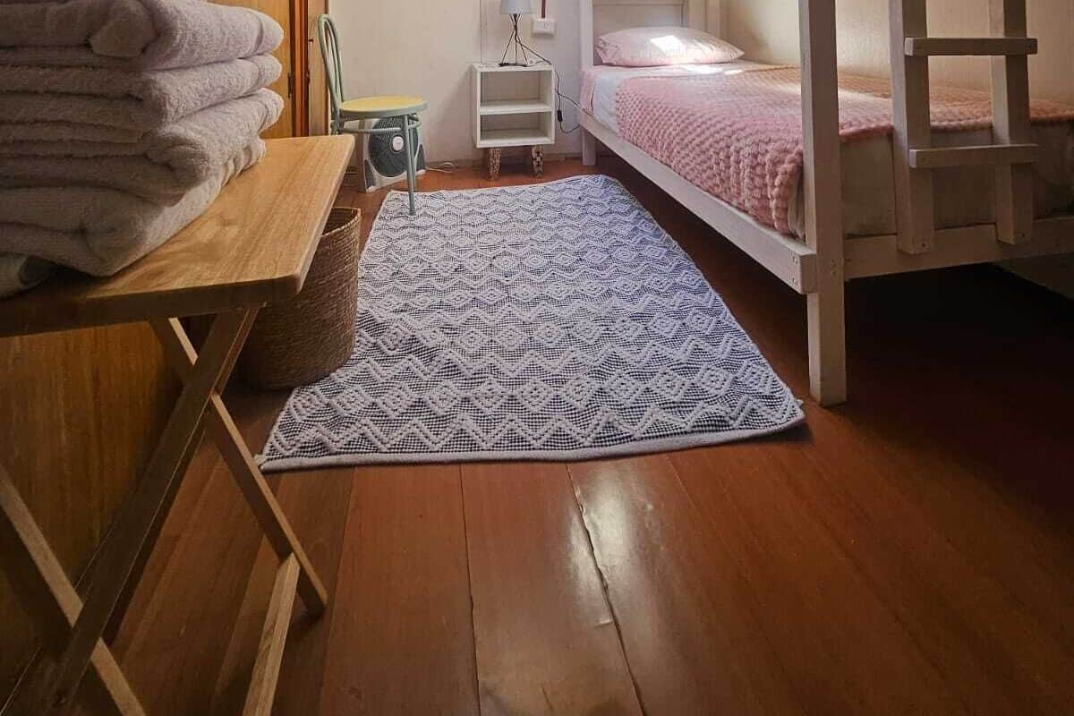 Um quarto de sótão acolhedor com beliche, uma escrivaninha de madeira com uma pilha de toalhas, um tapete estampado e um claraboia.