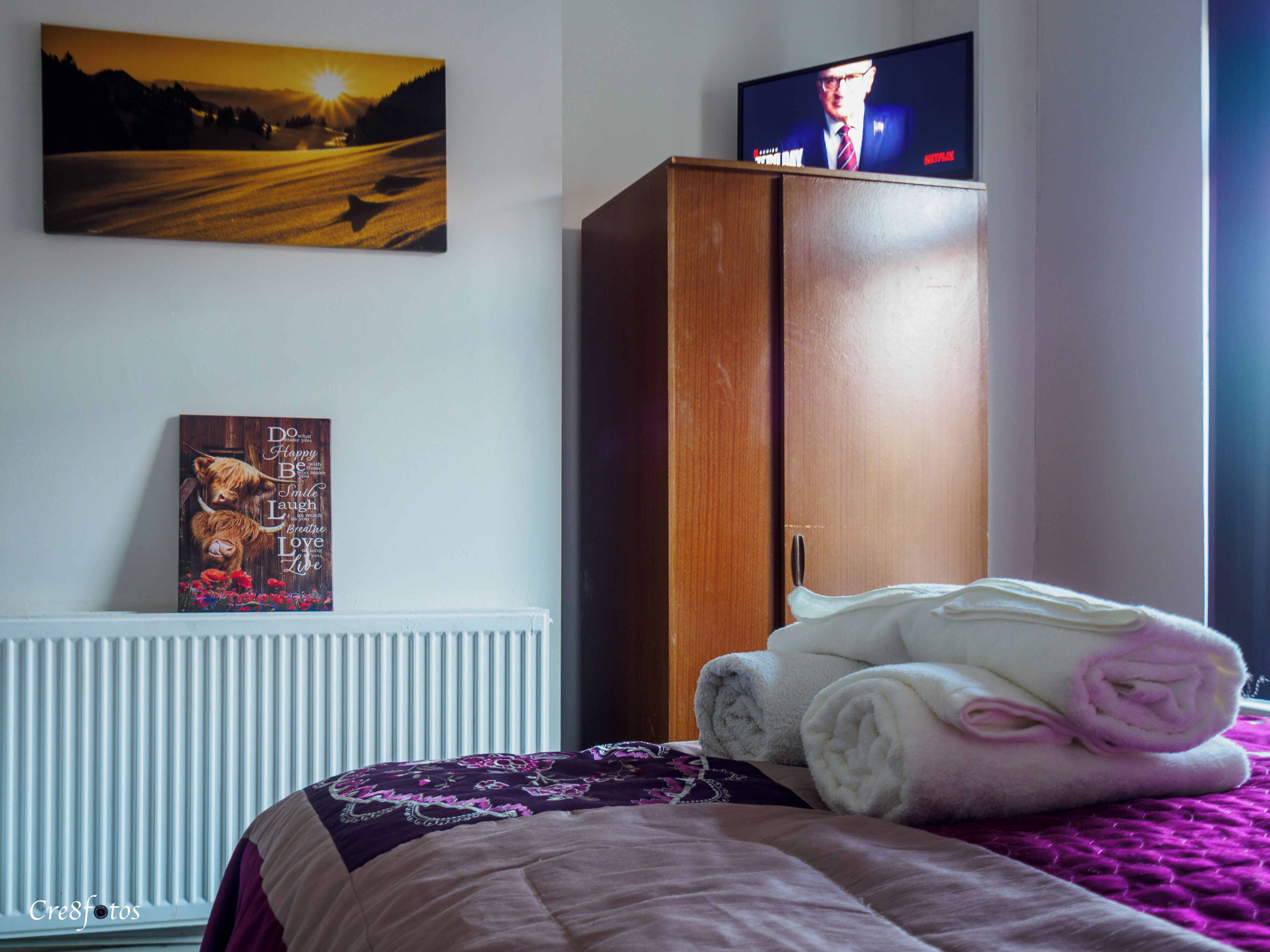 Quarto de hotel com cama, guarda-roupa de madeira, um quadro e televisão na parede.