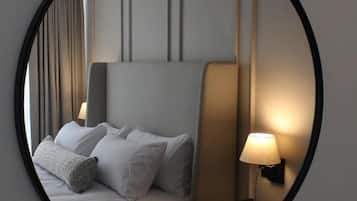 Um espelho circular reflete uma cama bem arrumada com almofadas e uma mesa de cabeceira com abajur.