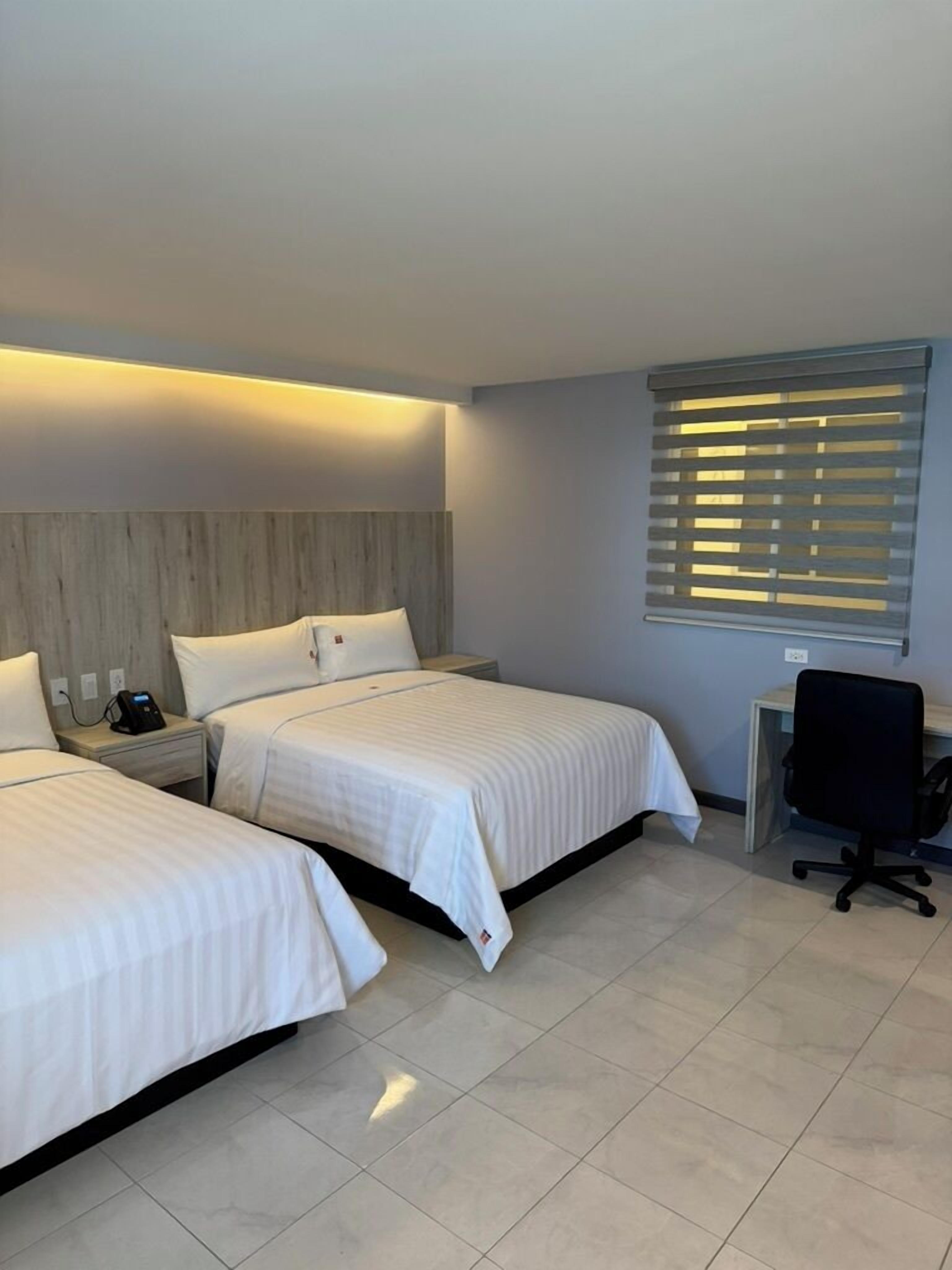 Quarto de hotel com duas camas, uma escrivaninha e uma cadeira.