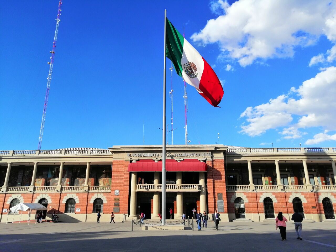 Um edifício grande com um mastro de bandeira em destaque, um toldo vermelho e um céu azul claro.