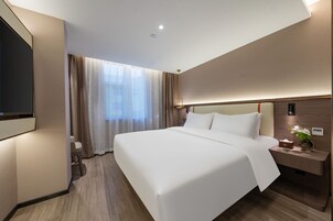Quarto de hotel moderno com uma cama grande, uma mesinha de cabeceira com abajur e uma TV fixada na parede.