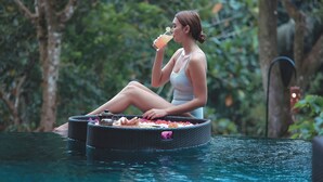 Uma pessoa sentada em uma plataforma flutuante em uma piscina, cercada por vegetação exuberante.