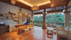 Uma área de pátio ampla com teto de madeira, balcão de bar, assentos e vista para vegetação exuberante.