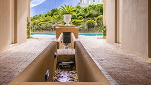 Um corredor com um elemento aquático, vista para uma montanha e piscina ao fundo.