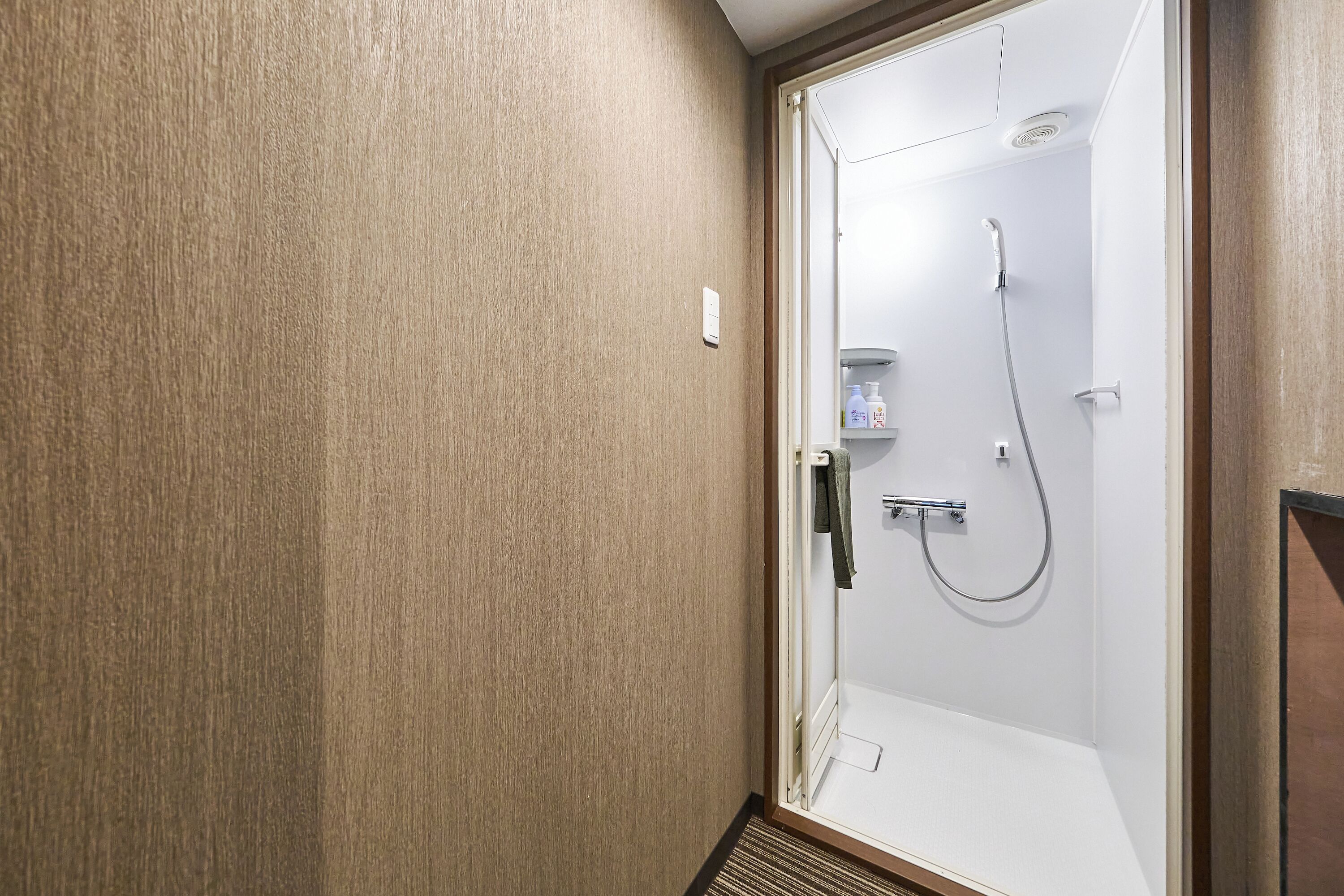 Casa de banho de hotel com chuveiro, porta-toalhas e um pequeno armário com artigos de higiene pessoal.