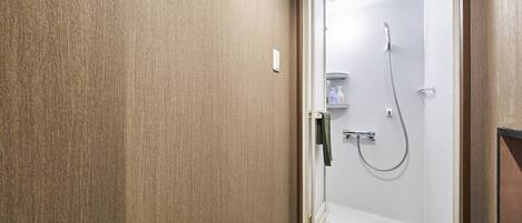 Casa de banho de hotel com chuveiro, porta-toalhas e um pequeno armário com artigos de higiene pessoal.