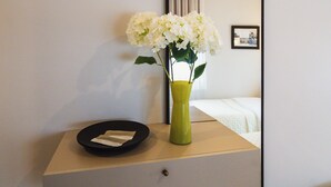 Quarto de hotel com mesa de cabeceira, espelho e um vaso com flores.