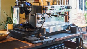 Máquina de café com visor digital, moedor de café e vários copos e utensílios sobre um balcão.