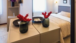 Quarto de hotel moderno com cama, mesas de cabeceira, um espelho e um vaso com flores vermelhas.