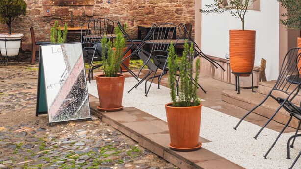 Uma área de estar ao ar livre com paredes de pedra, plantas em vasos e uma placa com a inscrição