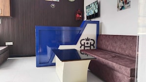 Uma área de recepção com uma mesa azul e branca, um sofá roxo, uma TV e uma obra de arte pendurada na parede.