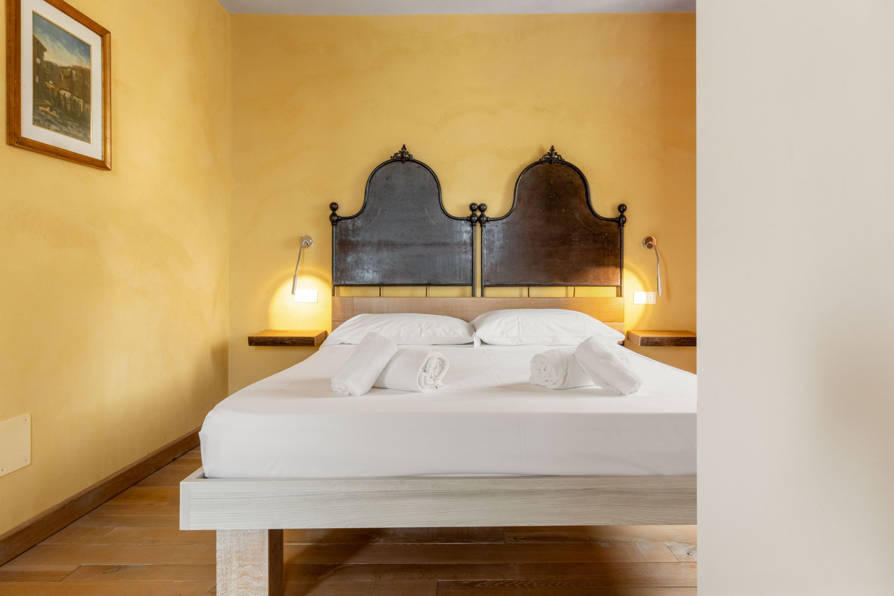 Cama bem arrumada com cabeceira de madeira, lençóis brancos e duas luminárias de cabeceira.