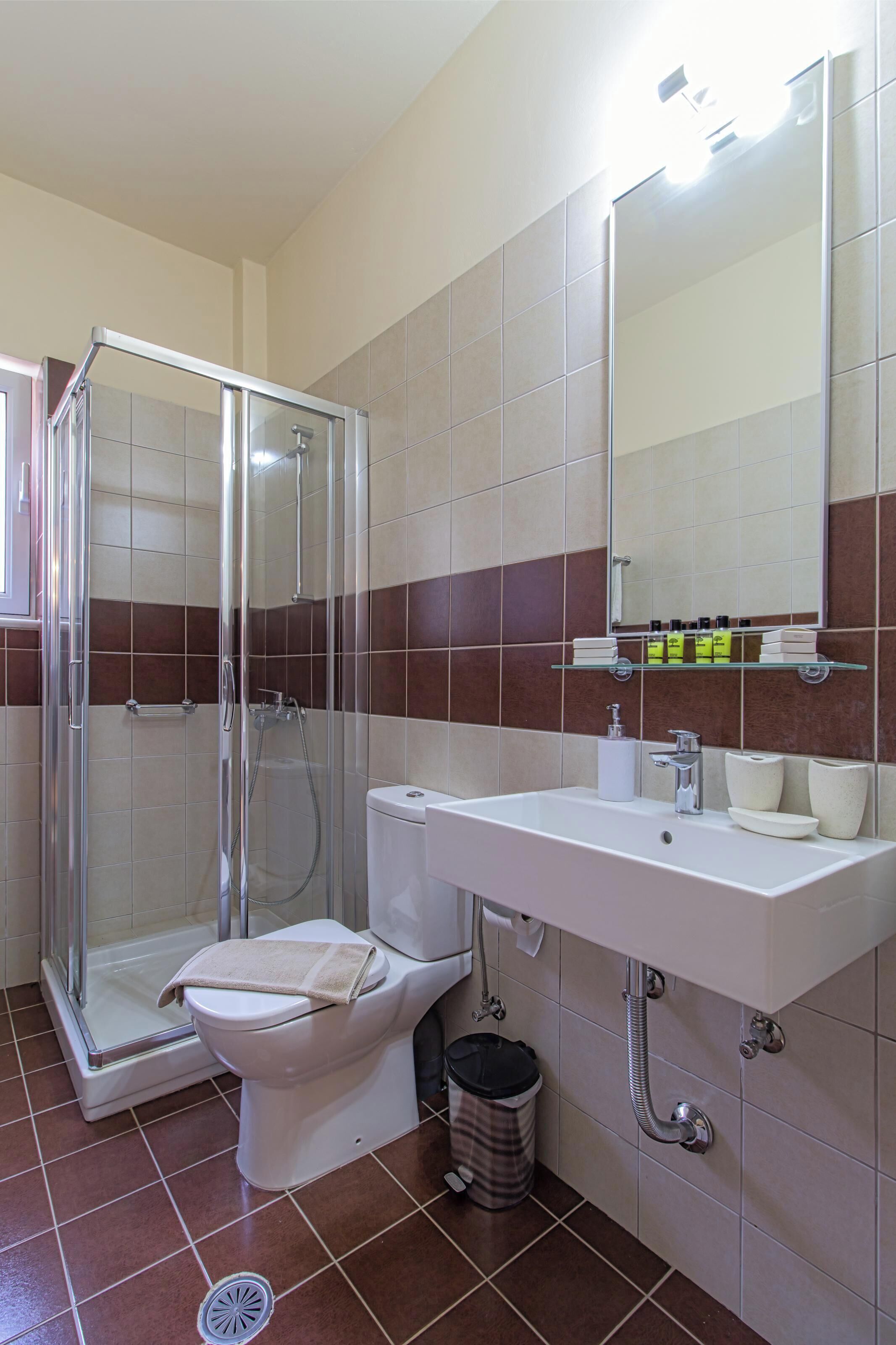 Casa de banho com cabine de duche com vidro, sanita, lavatório com espelho e um lixo.