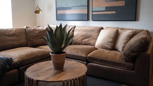 Uma sala de estar moderna com um sofá em couro marrom, uma mesa de centro redonda de madeira e uma grande planta de agave.