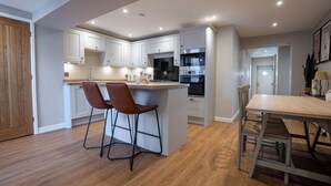 Uma cozinha moderna com armários brancos, uma ilha central com banquetas, uma área de refeições com mesa e cadeiras, e eletrodomésticos embutidos.