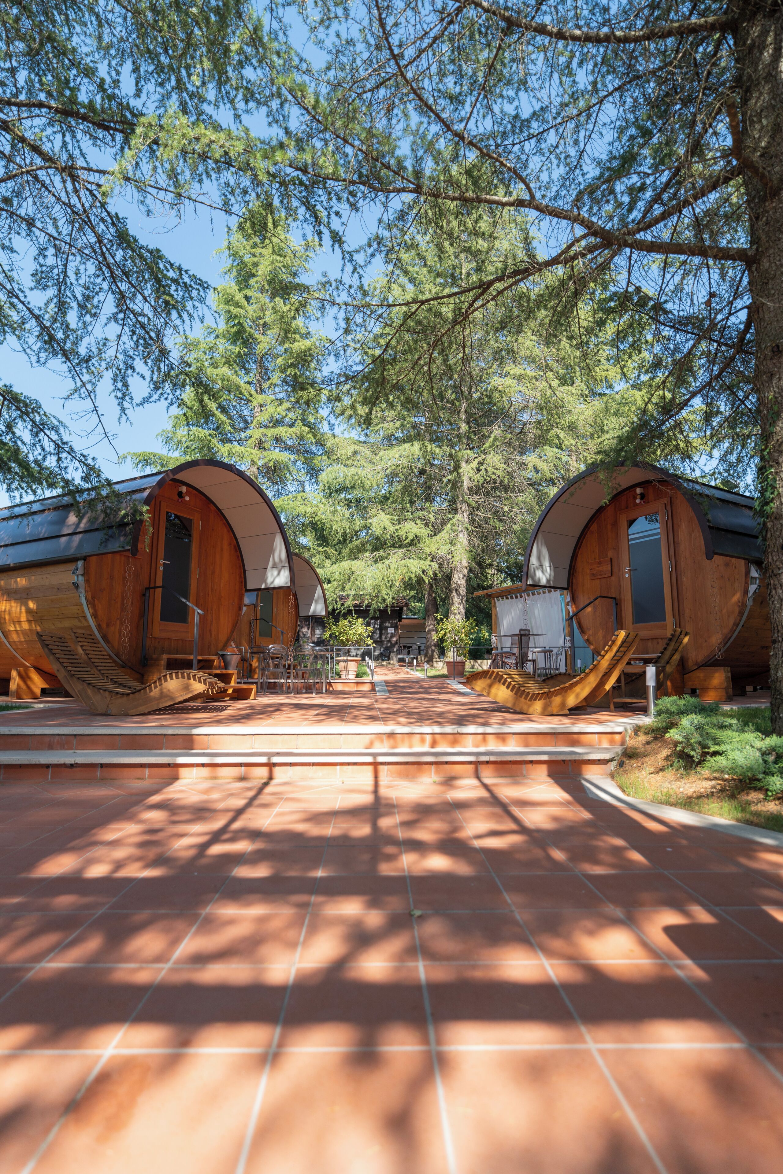 Duas cabanas de madeira com telhados curvos, um caminho central e árvores ao redor.