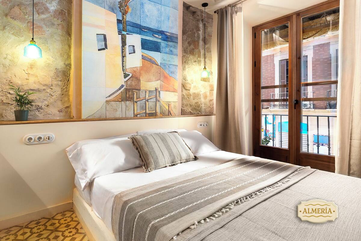 Quarto com cama, pintura, janela com cortinas e vista para o exterior.