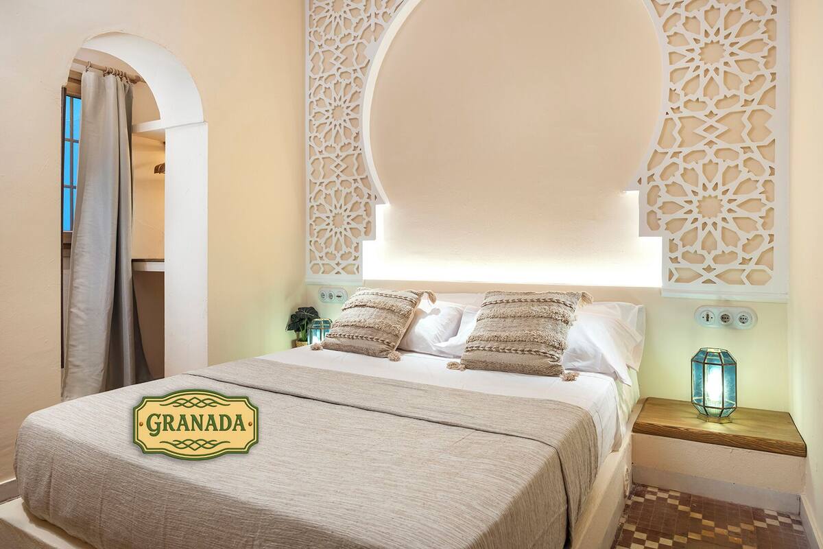 Quarto de hotel com cama, painéis decorativos na parede, mesa de cabeceira com abajur e uma placa na cama.
