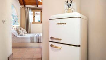 Quarto compacto com uma cama, geladeira branca e ventilador de teto.