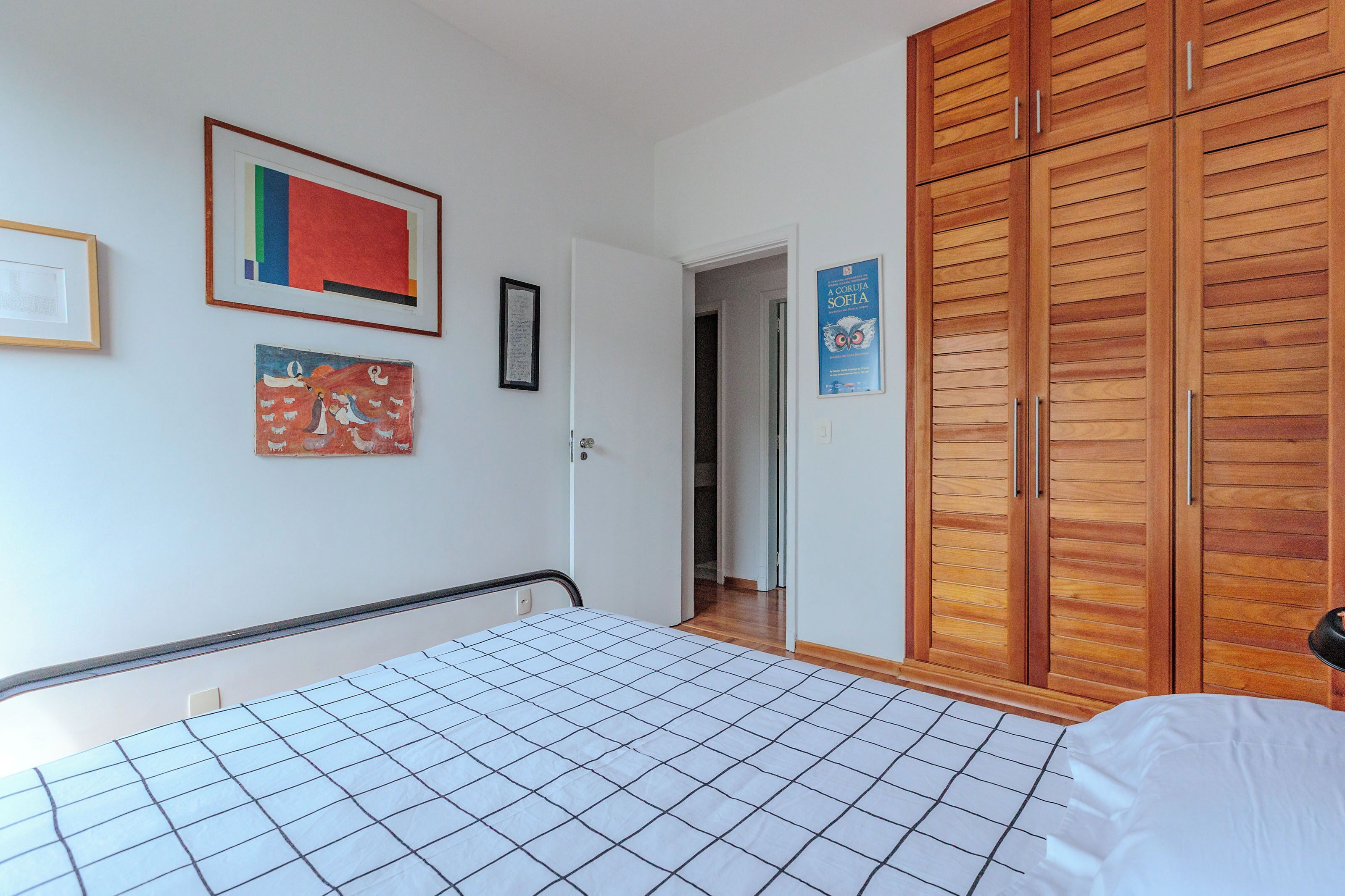 Quarto com cama, guarda-roupa de madeira e quadro na parede.