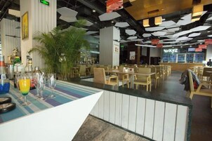 Interior de restaurante com área de bar, assentos e uma grande planta.