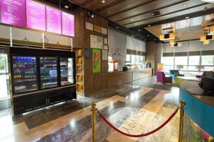 Um saguão de hotel com balcão de recepção, refrigerador com bebidas e piso de mármore.
