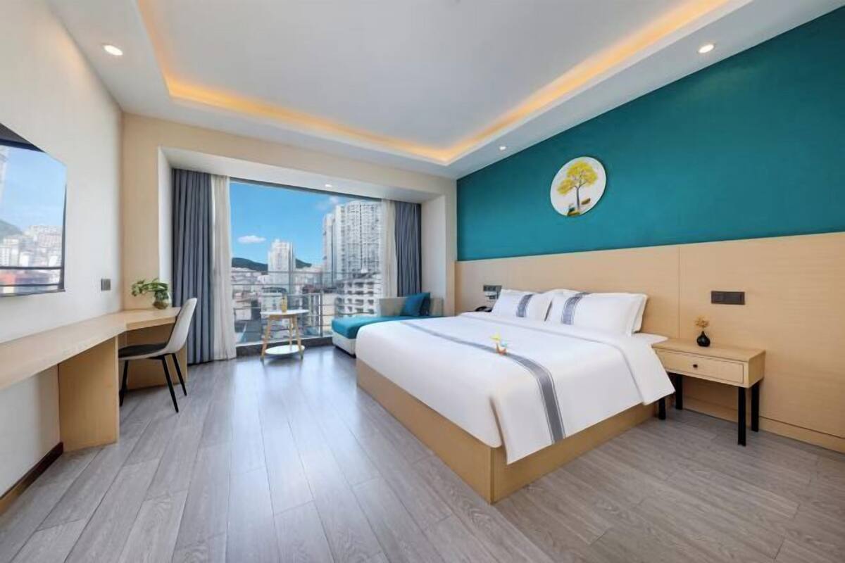 Quarto de hotel moderno com uma cama grande, uma escrivaninha e vista para a cidade.