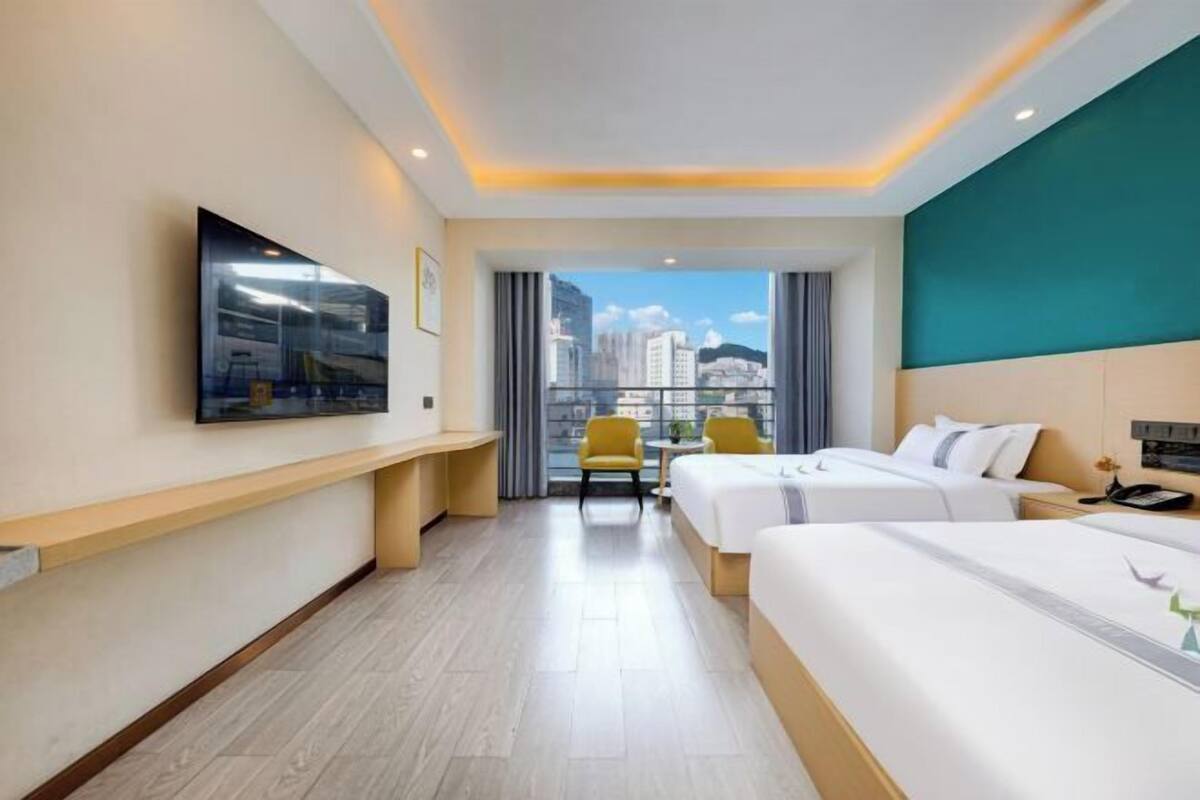 Quarto de hotel com duas camas, televisão, escrivaninha e vista para a cidade.