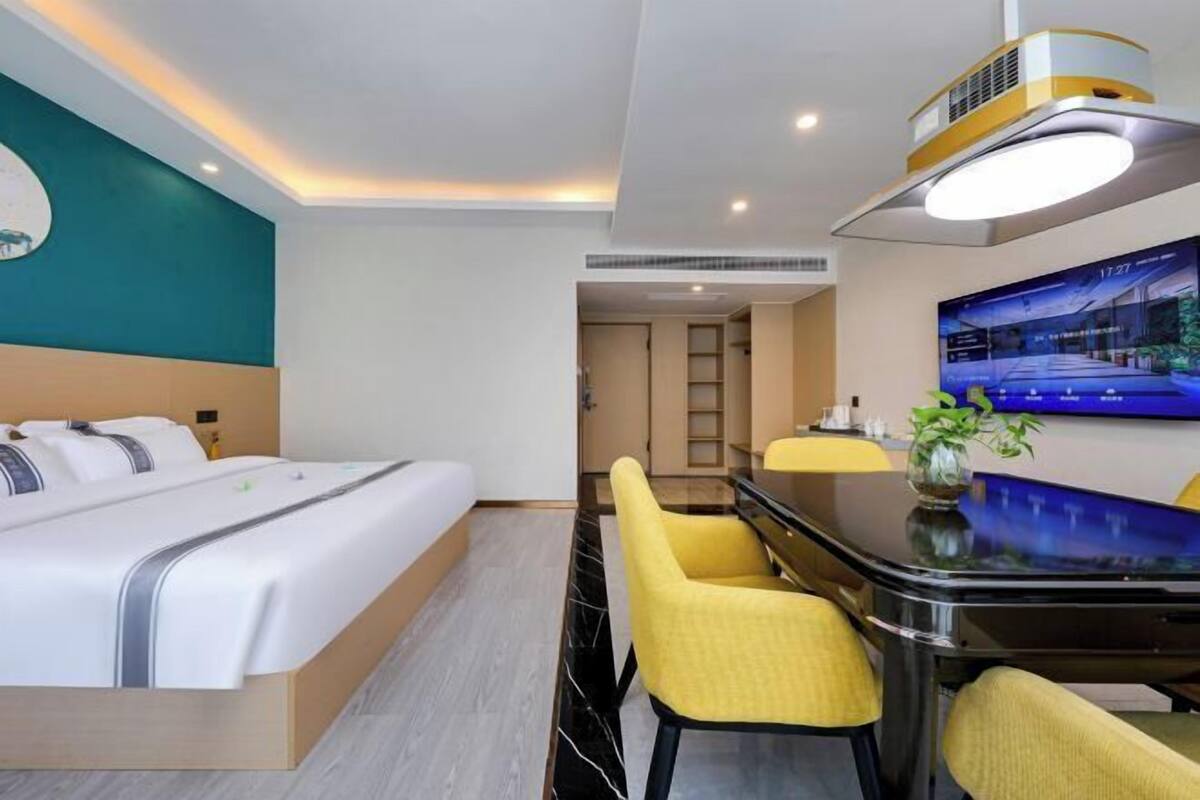 Quarto de hotel com cama, mesa de jantar com cadeiras, televisão e unidade de ar condicionado no teto.