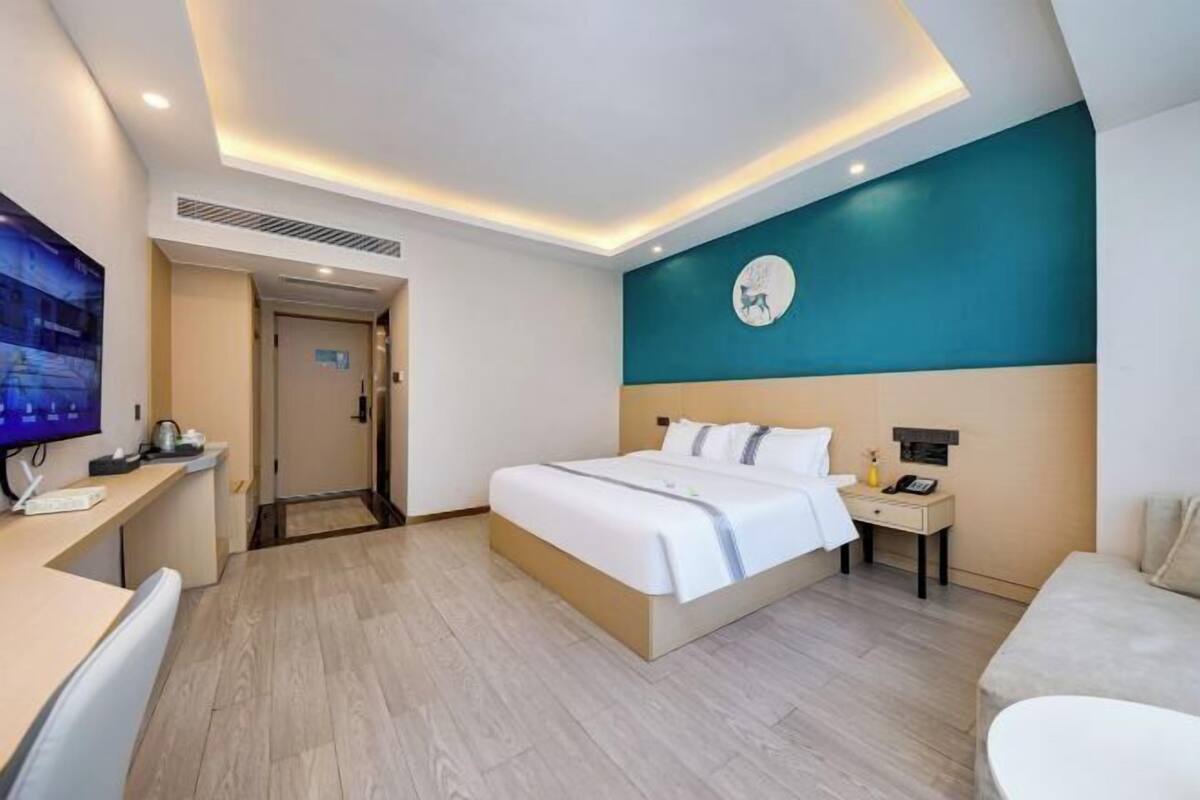 Quarto de hotel com cama, mesa de cabeceira, escrivaninha e televisão.
