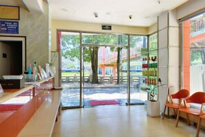 Uma área de recepção com balcão, entrada por porta de vidro e espaço de espera com cadeiras.