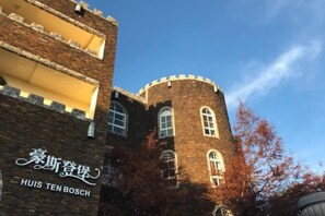 Um edifício de tijolos com uma torre e janelas em arco, com a inscrição 'HUIS TEN BOSCH'.