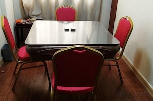 Uma mesa retangular para refeições com quatro cadeiras, cada uma com assento acolchoado em vermelho e moldura dourada.