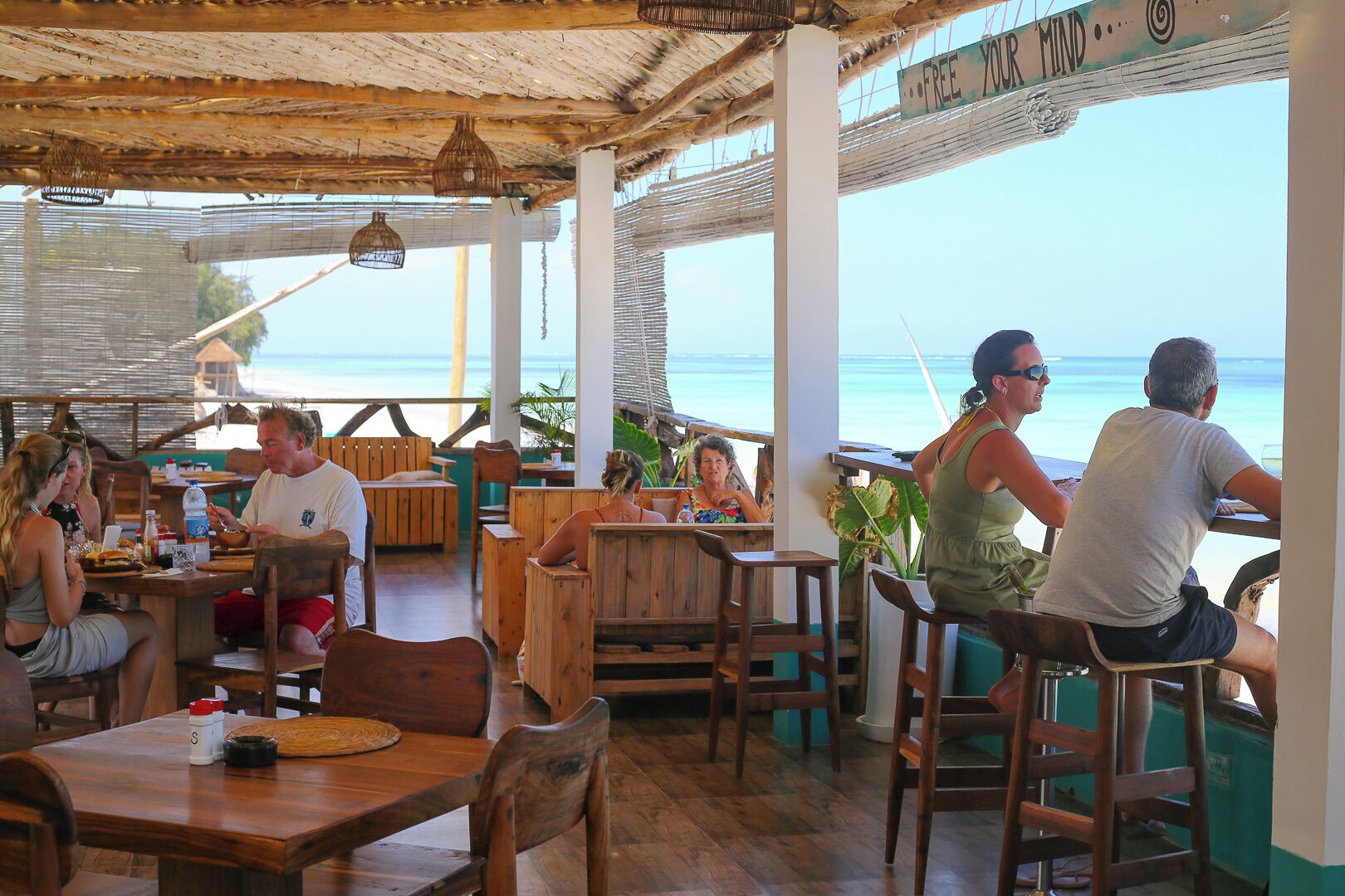 Restaurante à beira-mar com mobiliário de madeira e vista para o oceano.