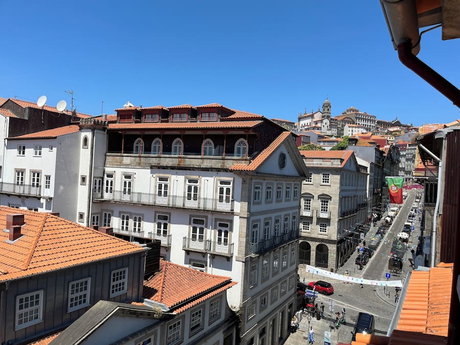 Vista da rua de uma cidade com edifícios históricos, céu azul claro e uma bandeira em um mastro.