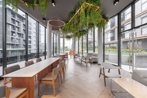 Uma sala de reunião moderna com mesas compridas, cadeiras, janelas amplas e plantas penduradas.