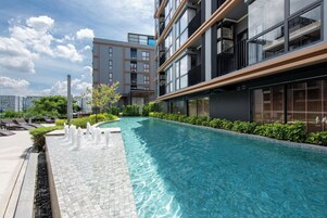 Uma área de piscina moderna com piscina azul cristalina, cadeiras de descanso e um edifício com varandas.