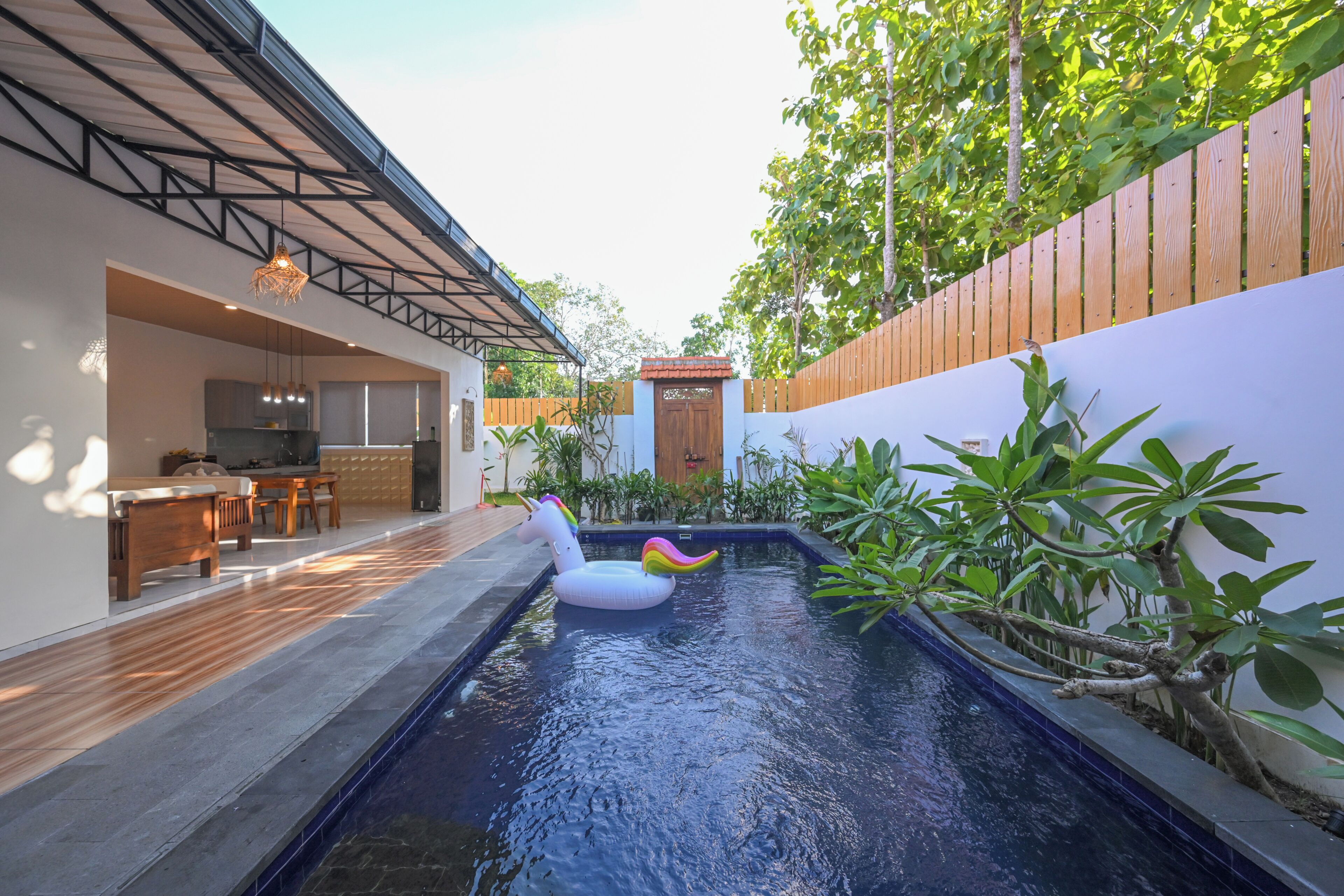 Uma piscina com um flutuador de unicórnio, cercada por uma cerca de madeira e vegetação exuberante.