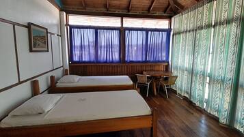 Quarto com duas camas de madeira, uma mesinha e uma janela com cortinas.