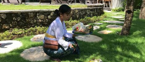 Uma pessoa sentada na grama em uma área de jardim, com cadeiras de descanso e um muro de pedra ao fundo.