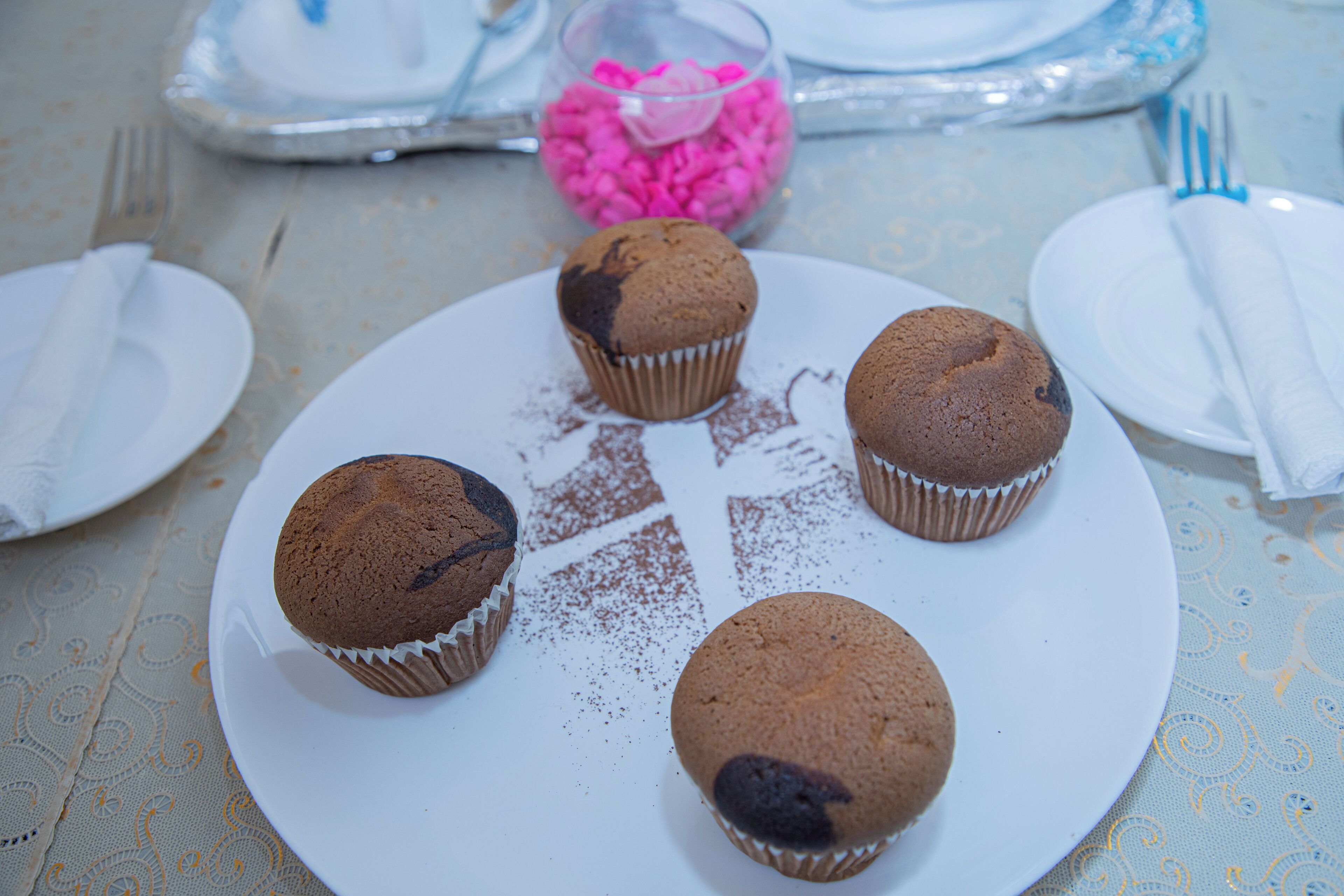 Um prato com quatro muffins sobre uma mesa com toalha de mesa estampada.