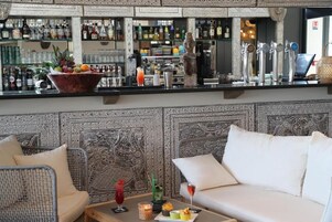 Uma área de bar com diversos tipos de garrafas, uma cesta de frutas e um espaço de estar com sofá e cadeiras.