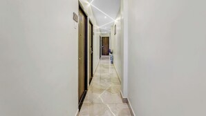 Um corredor com piso lustroso, paredes brancas e luminária moderna.