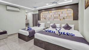 Quarto de hotel com duas camas, um ventilador de teto, iluminação embutida, aparelho de ar condicionado, painel decorativo na parede e uma pequena mesa com um vaso.