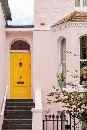 Um edifício rosa com uma porta amarela vibrante, uma escadaria e um corrimão branco.